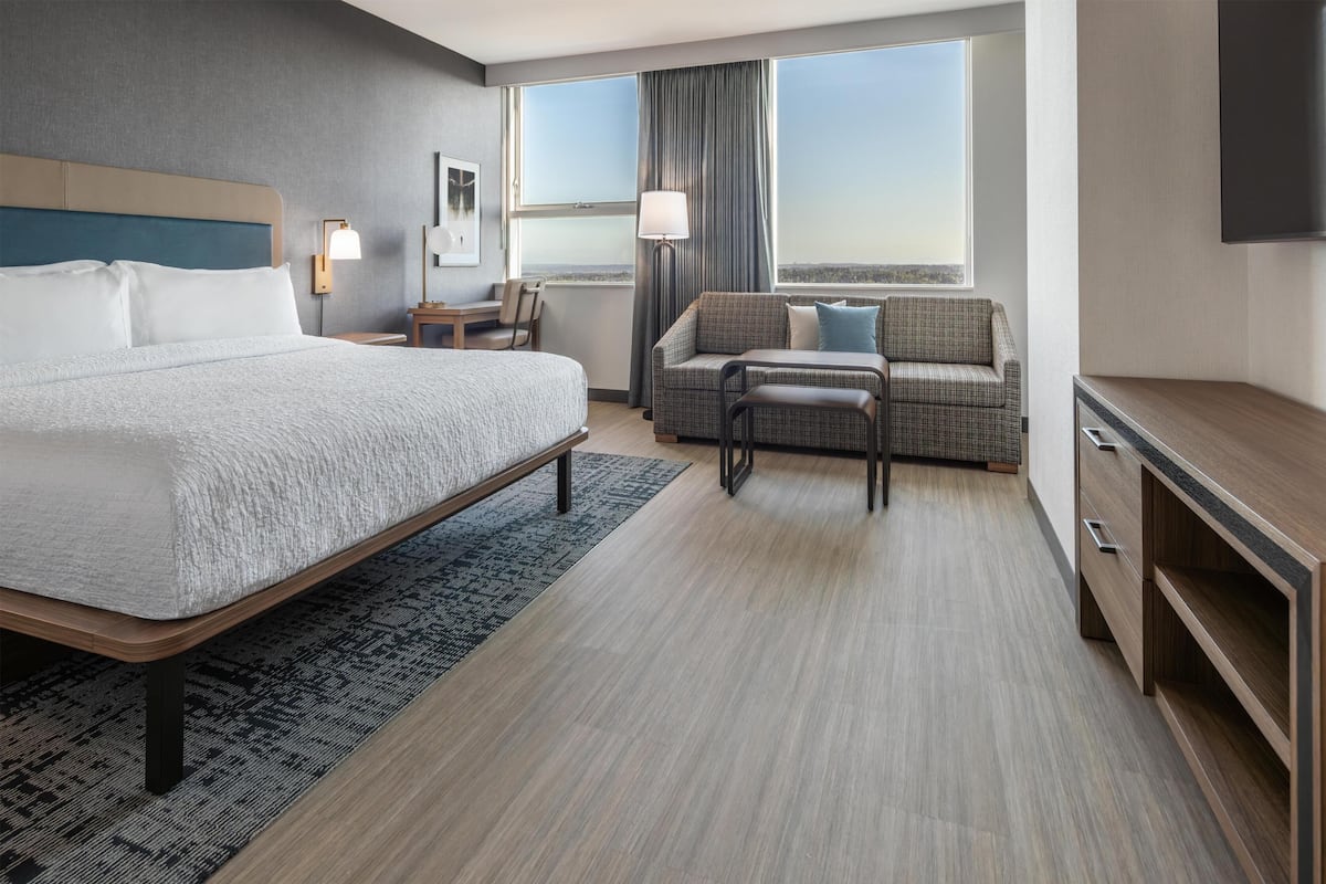 Quarto de hotel com uma cama grande, um sofá, uma escrivaninha e uma televisão.