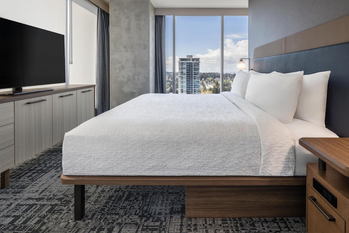 Quarto de hotel moderno com uma cama grande, televisão de tela plana e vista para a cidade.