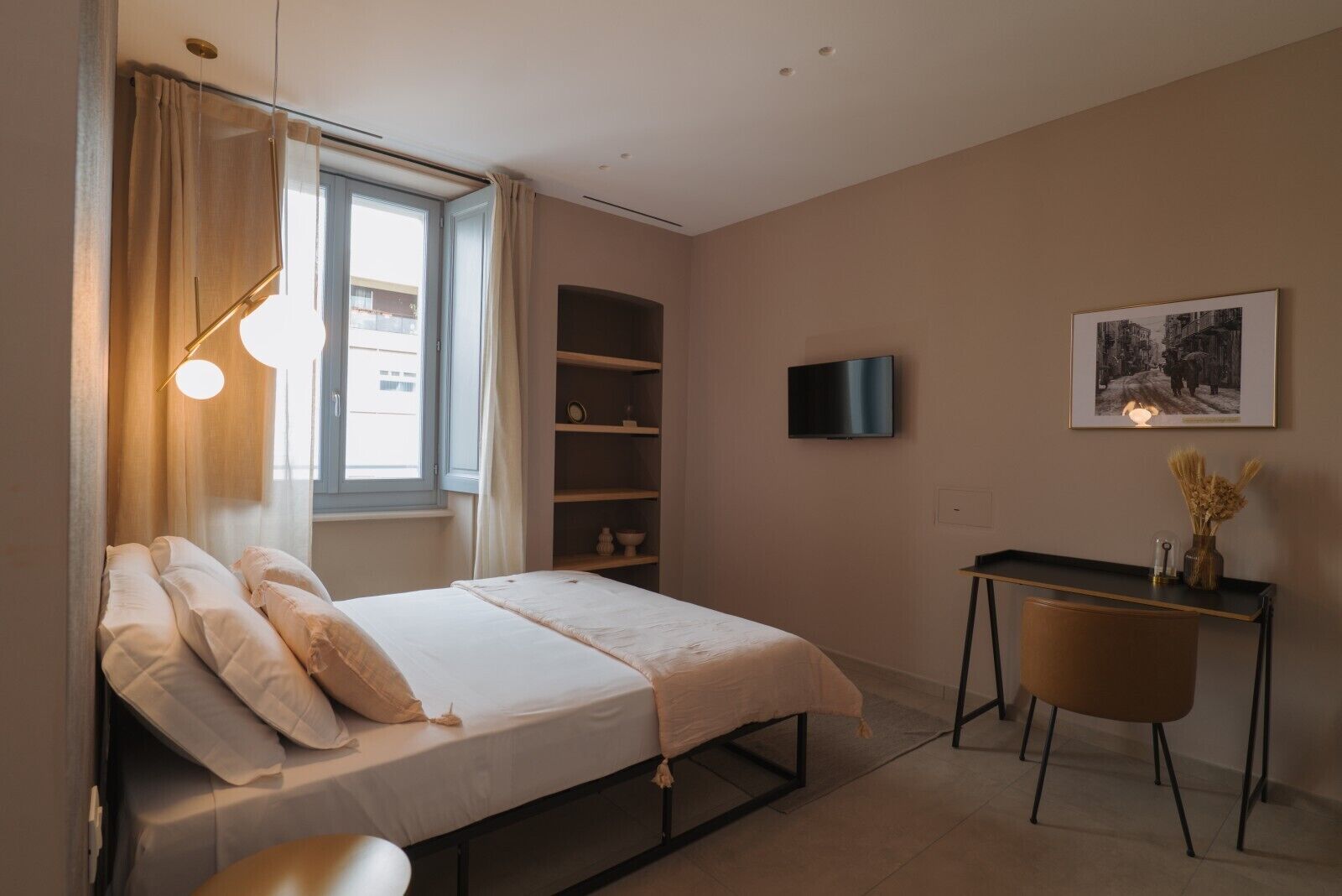 Quarto com cama, escrivaninha, cadeira, televisão e janela com cortinas.