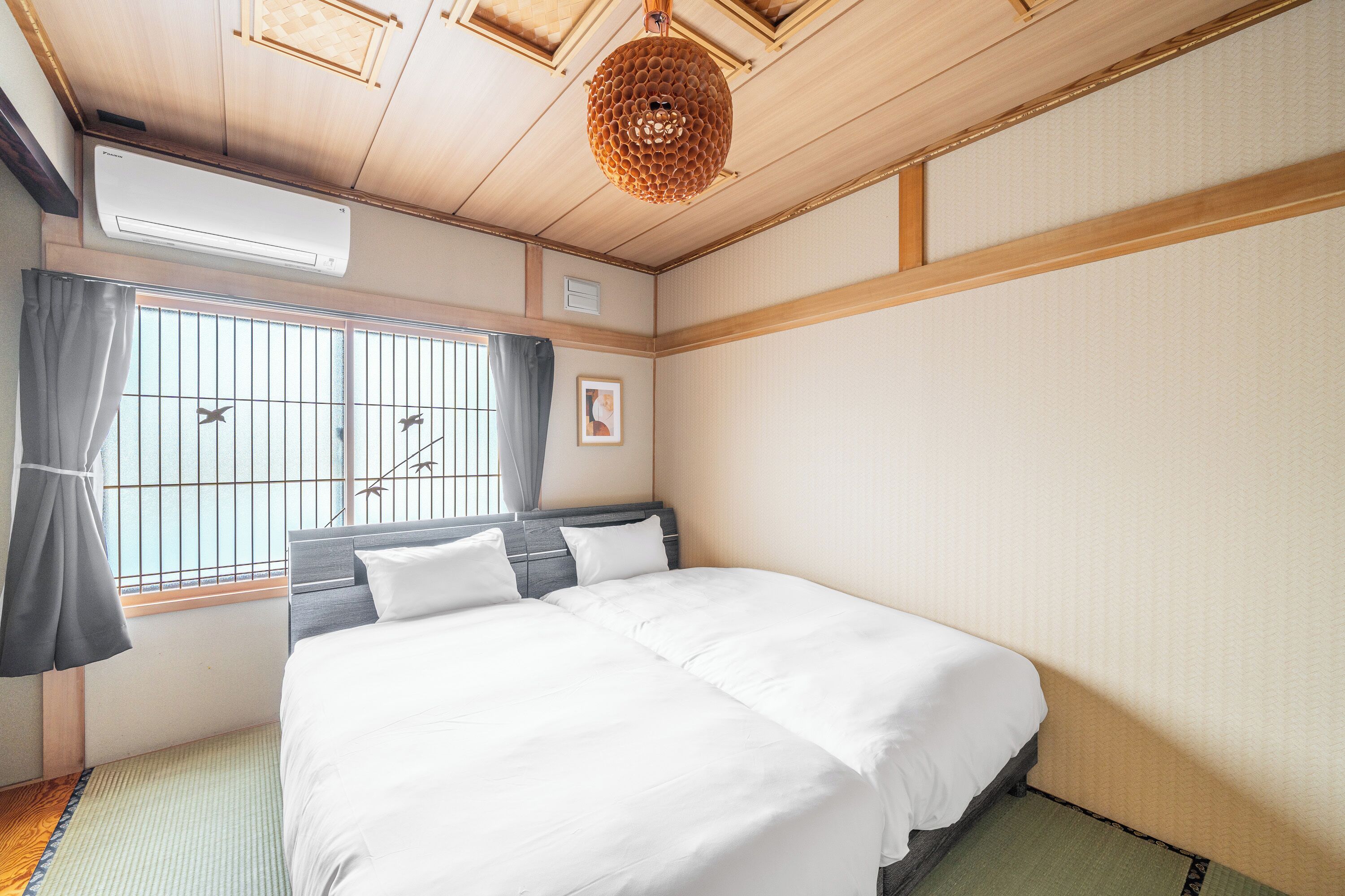 Um quarto em estilo japonês tradicional com piso de tatame, uma cama grande com roupa de cama branca, um ventilador de teto e uma janela com vidro gradeado.