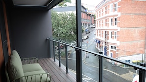 Uma varanda com vista para uma rua da cidade, uma cadeira verde e um edifício com a placa 