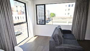 Uma sala de estar moderna com um sofá cinzento, uma poltrona branca e uma grande janela com vista para a paisagem urbana.