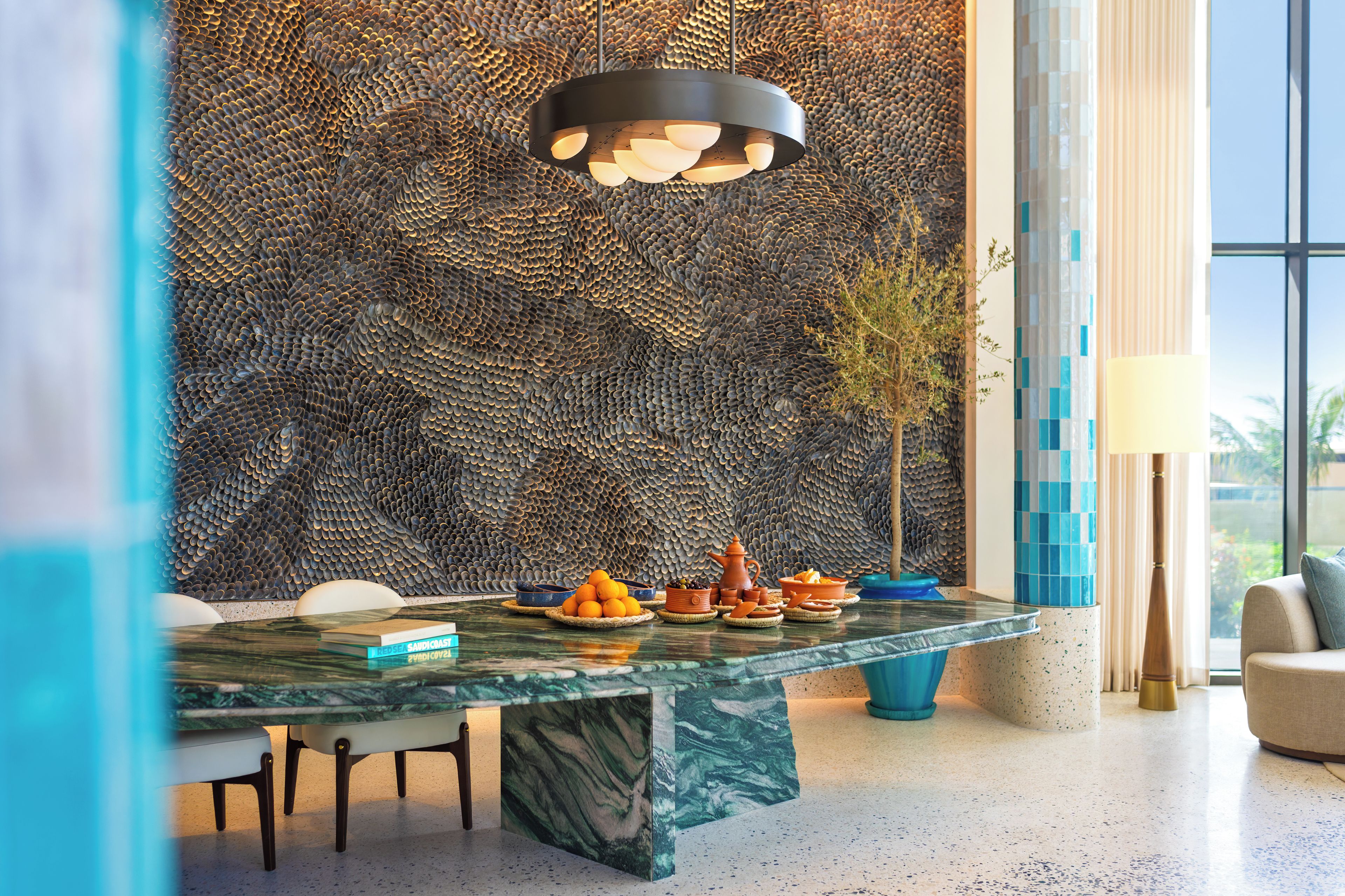 Uma sala de jantar moderna com mesa de mármore, parede com textura diferenciada e luminária contemporânea.