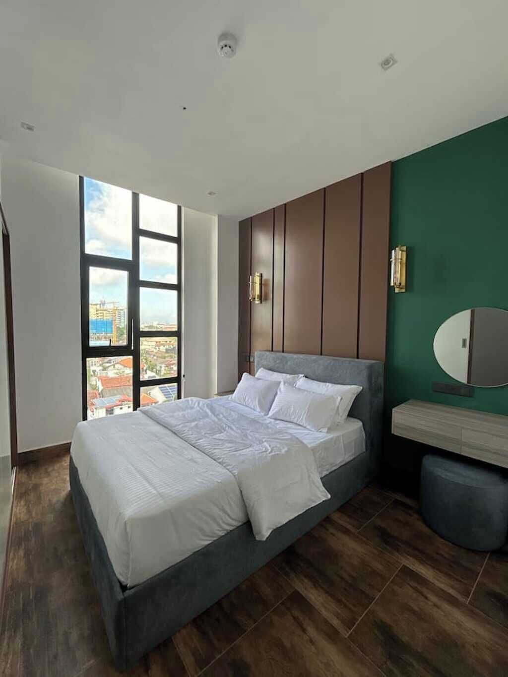 Um quarto moderno com uma cama grande, uma toucador com espelho e vista da cidade através de uma janela ampla.