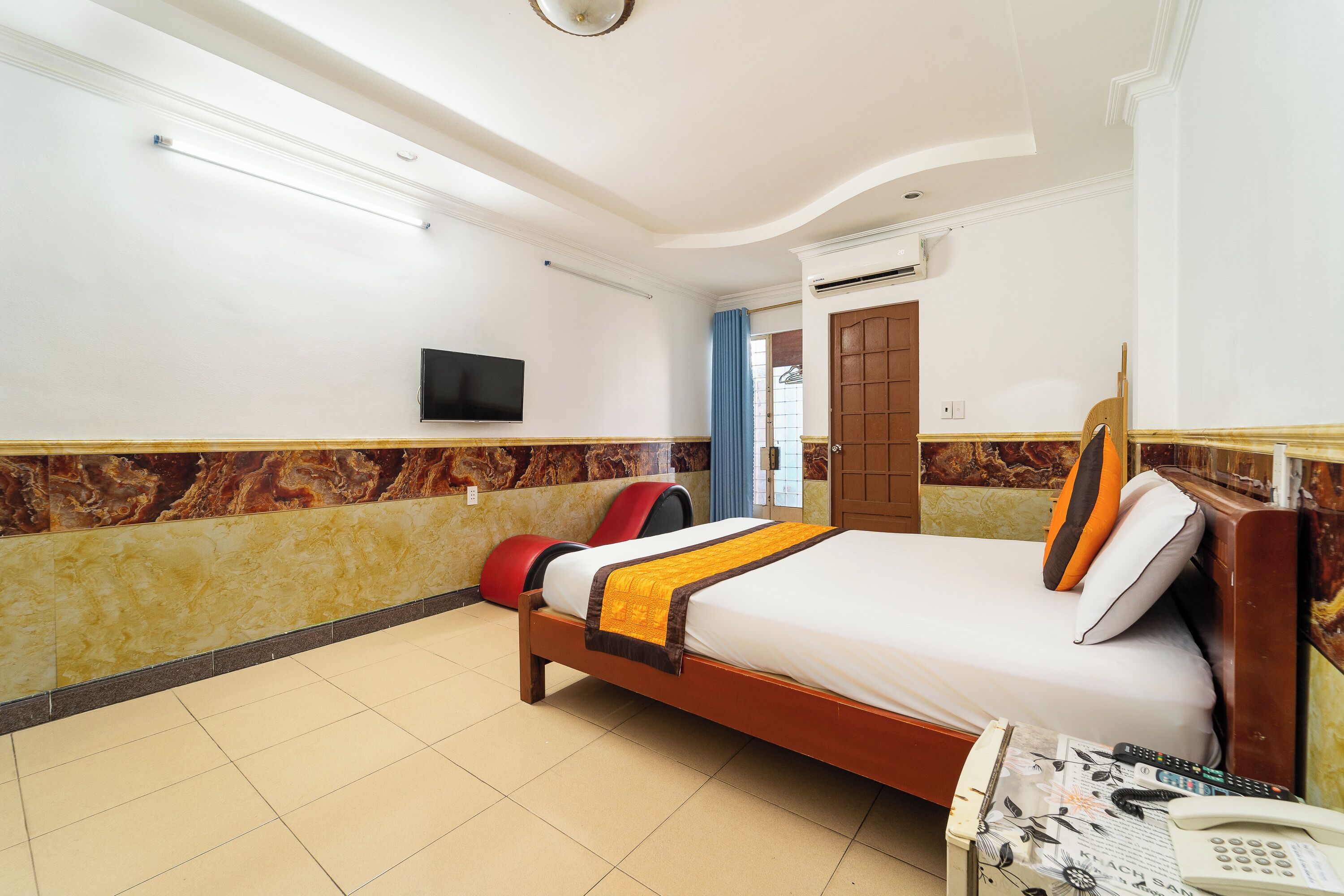 Quarto de hotel com cama, televisão na parede e telefone na mesinha de cabeceira.