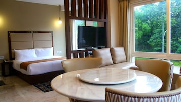 Quarto de hotel com uma cama, televisão, sofá e mesa.