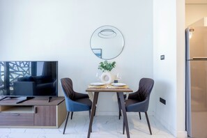 Uma sala de estar moderna com uma televisão de tela plana, uma mesa de jantar com duas cadeiras, um espelho e uma geladeira.