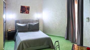 Quarto com uma cama, mesa de cabeceira, quadro na parede e janela com cortinas.