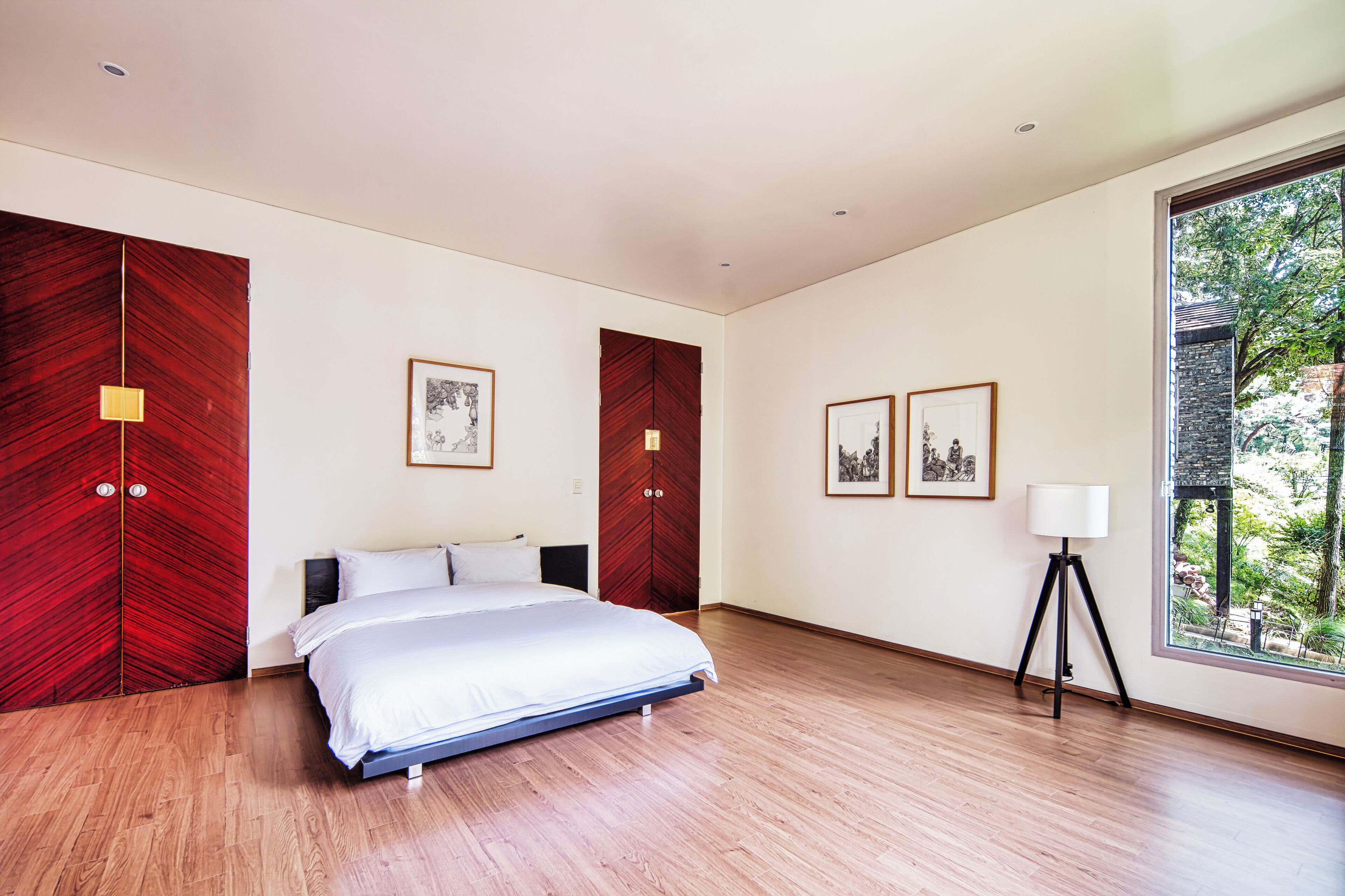 Quarto com cama, guarda-roupa de madeira, quadros emoldurados e janela com vista.