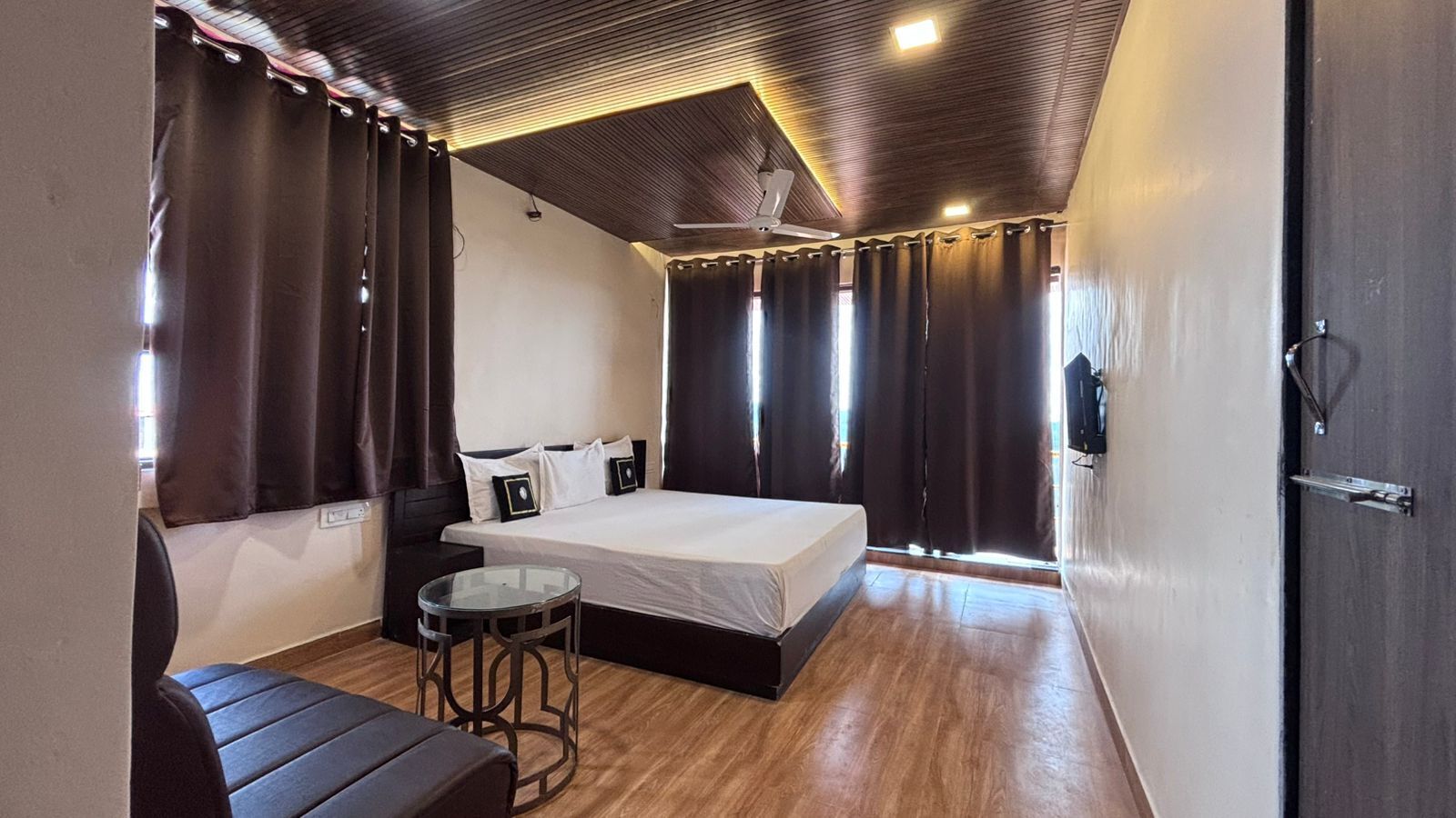 Quarto com cama, mesa redonda pequena, sofá e ventoinha no teto.