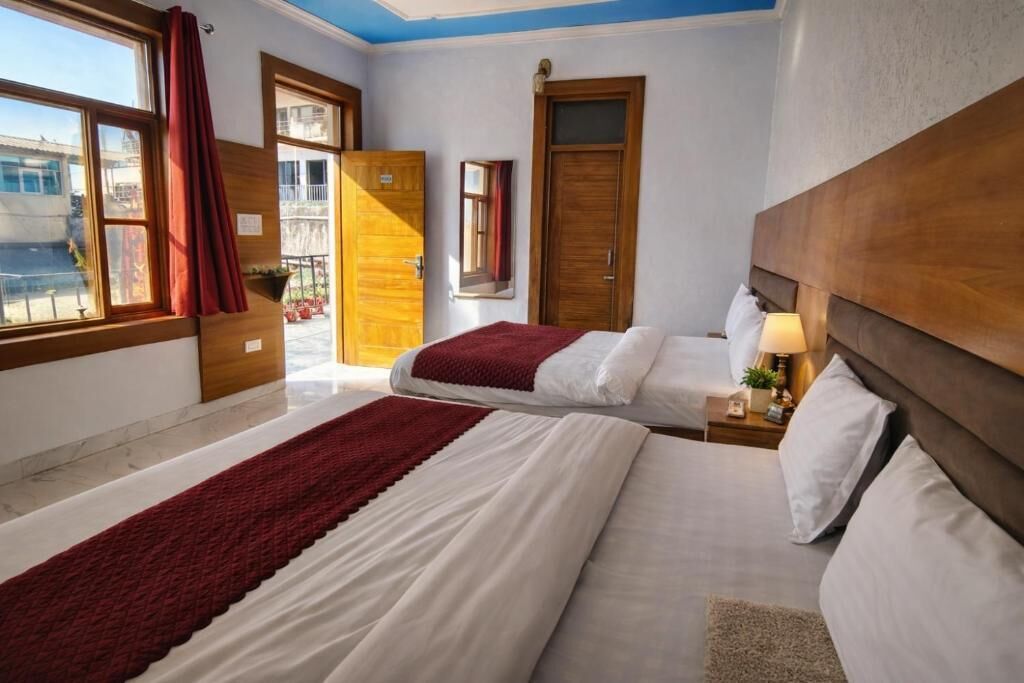 Quarto de hotel com duas camas, cabeceira de madeira, janela com vista e porta para o exterior.