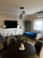 Uma sala de estar moderna com uma mesa de jantar redonda, uma televisão de tela plana na parede, uma grande planta em vaso e uma cama com cobertura azul.