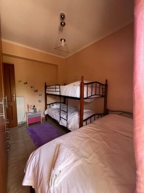 Quarto com beliches, uma pequena escrivaninha e um tapete roxo.