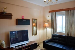 Uma sala de estar com televisão de tela plana, sofá, abajur e janela com cortinas.