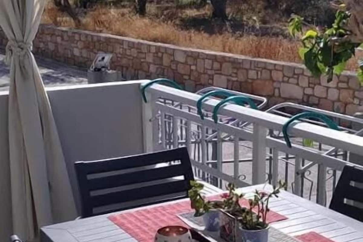 Uma área de pátio com uma mesa posta para dois, rodeada de cadeiras, e um muro de pedra ao fundo.