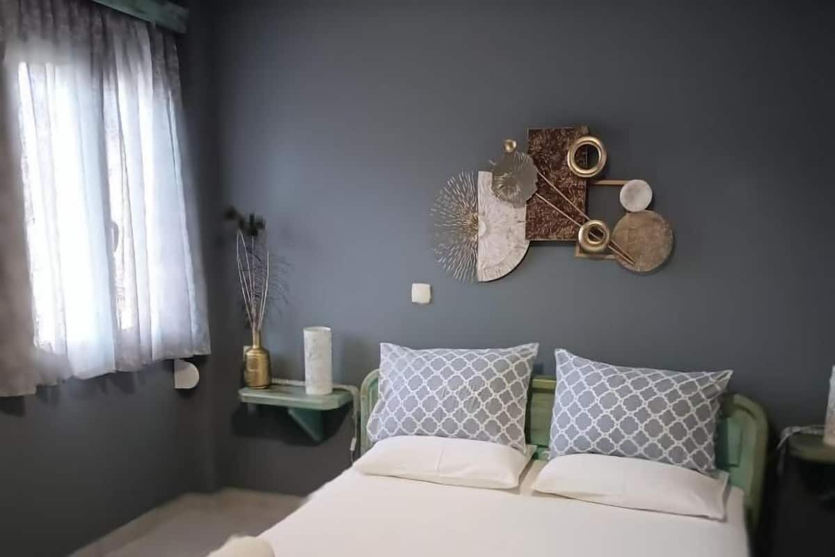 Cama bem arrumada com almofadas e toalhas, mesa de cabeceira com um vaso e um enfeite na parede.