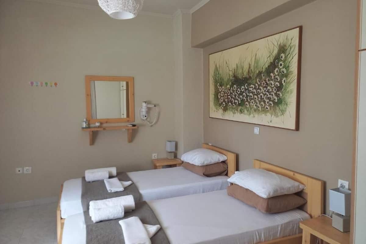 Quarto de hotel com duas camas, um quadro grande, um espelho e um lustre.