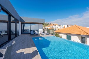 Uma área moderna à beira da piscina, com vista clara para a água, cadeiras de descanso e um edifício com amplas janelas de vidro.