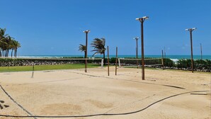 Uma quadra de voleibol de praia com rede, palmeiras e vista para o oceano.