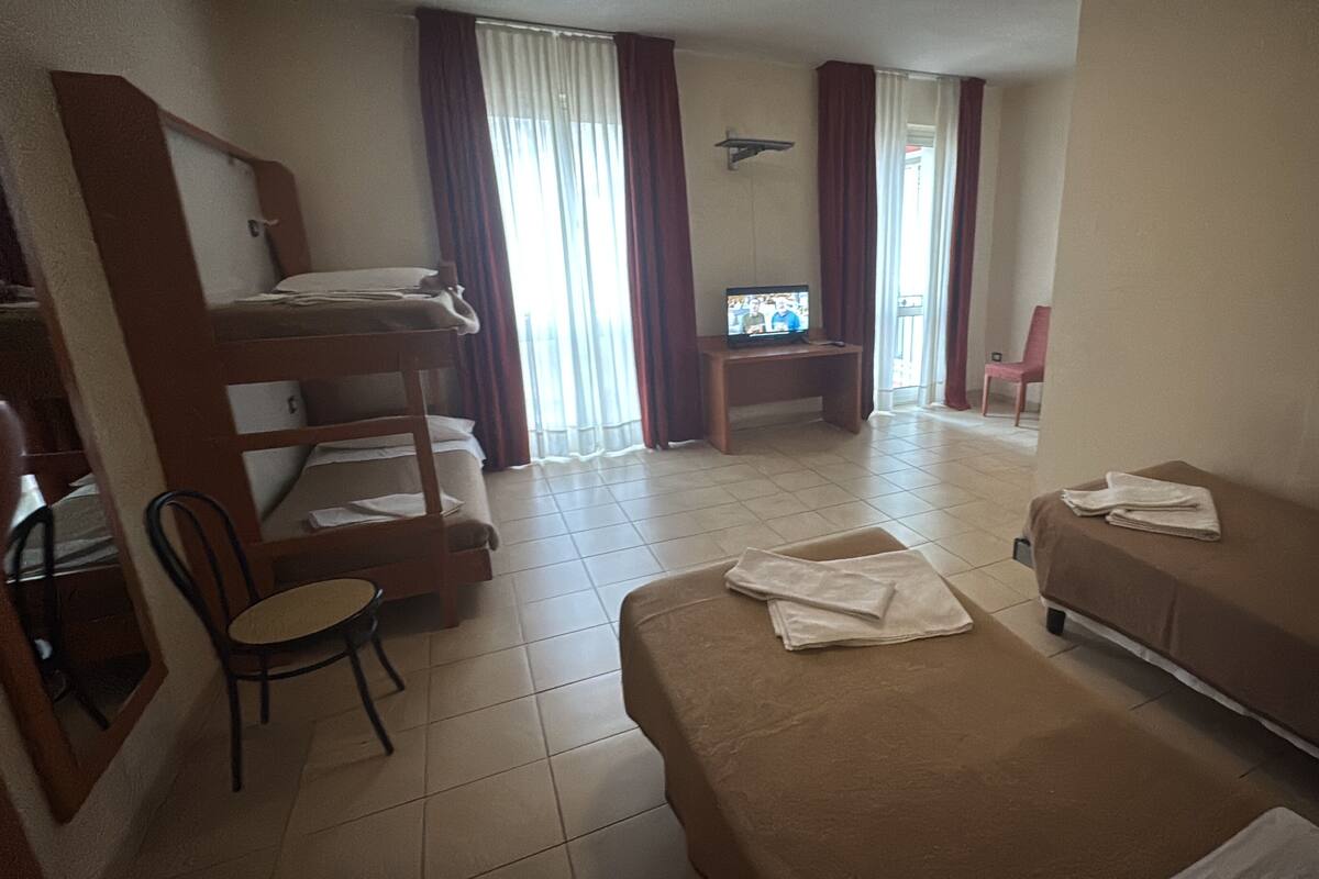 Quarto de hotel com beliches, sofá, televisão e uma cadeira.