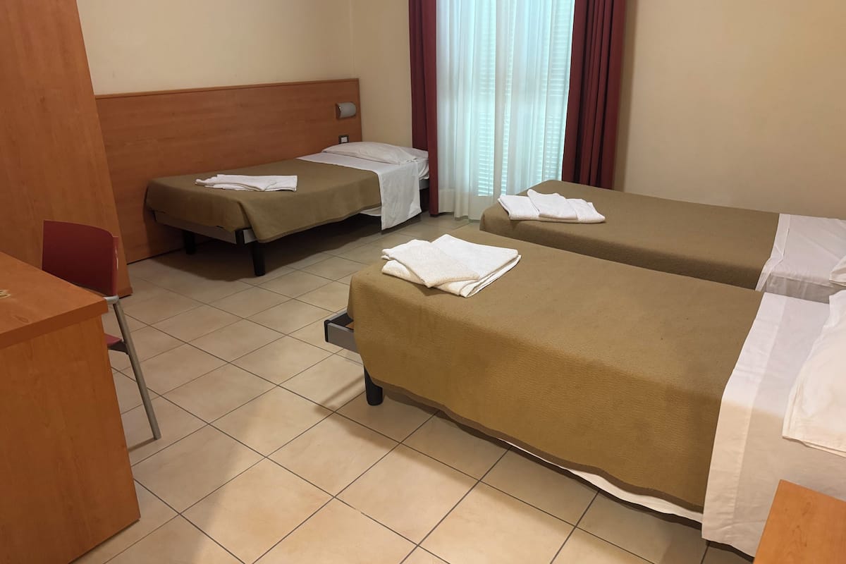 Quarto de hotel com duas camas de solteiro, cabeceira de madeira, uma mesinha e uma cadeira.
