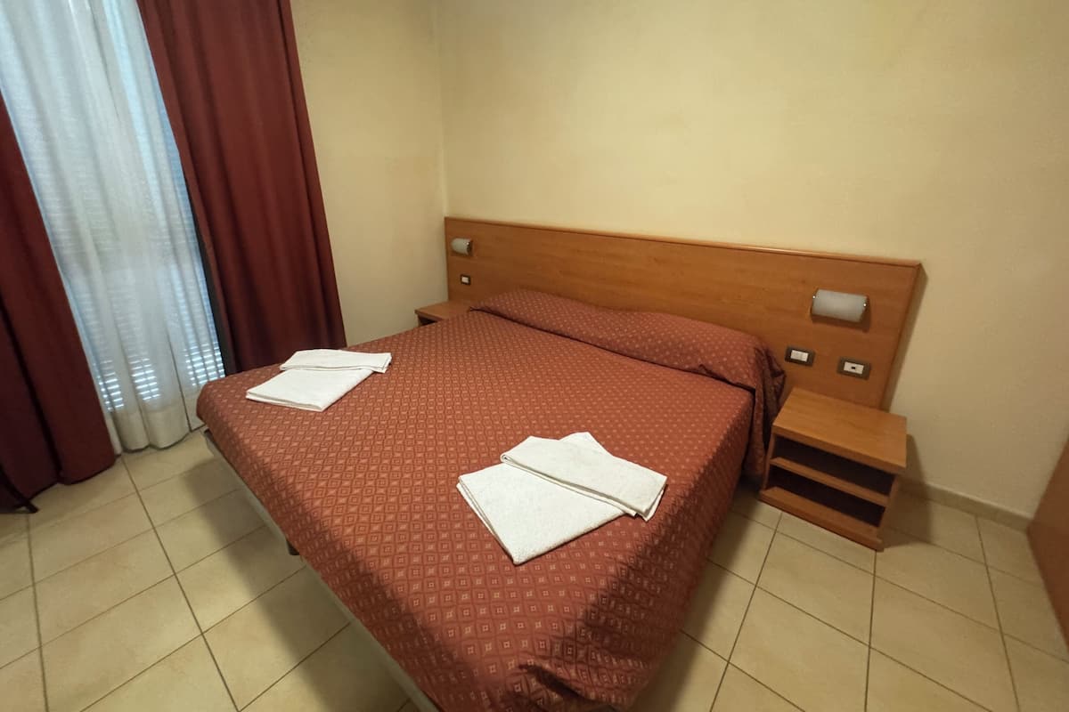 Uma cama de solteiro com cabeceira de madeira, duas mesas de cabeceira e uma janela com cortinas.