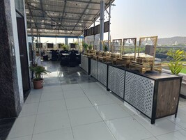 Uma área externa coberta com piso de azulejos, mesas e cadeiras, e detalhes decorativos.