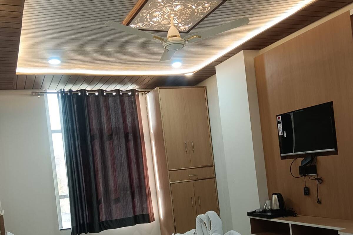Quarto de hotel com cama, televisão na parede, guarda-roupa e luminária no teto.