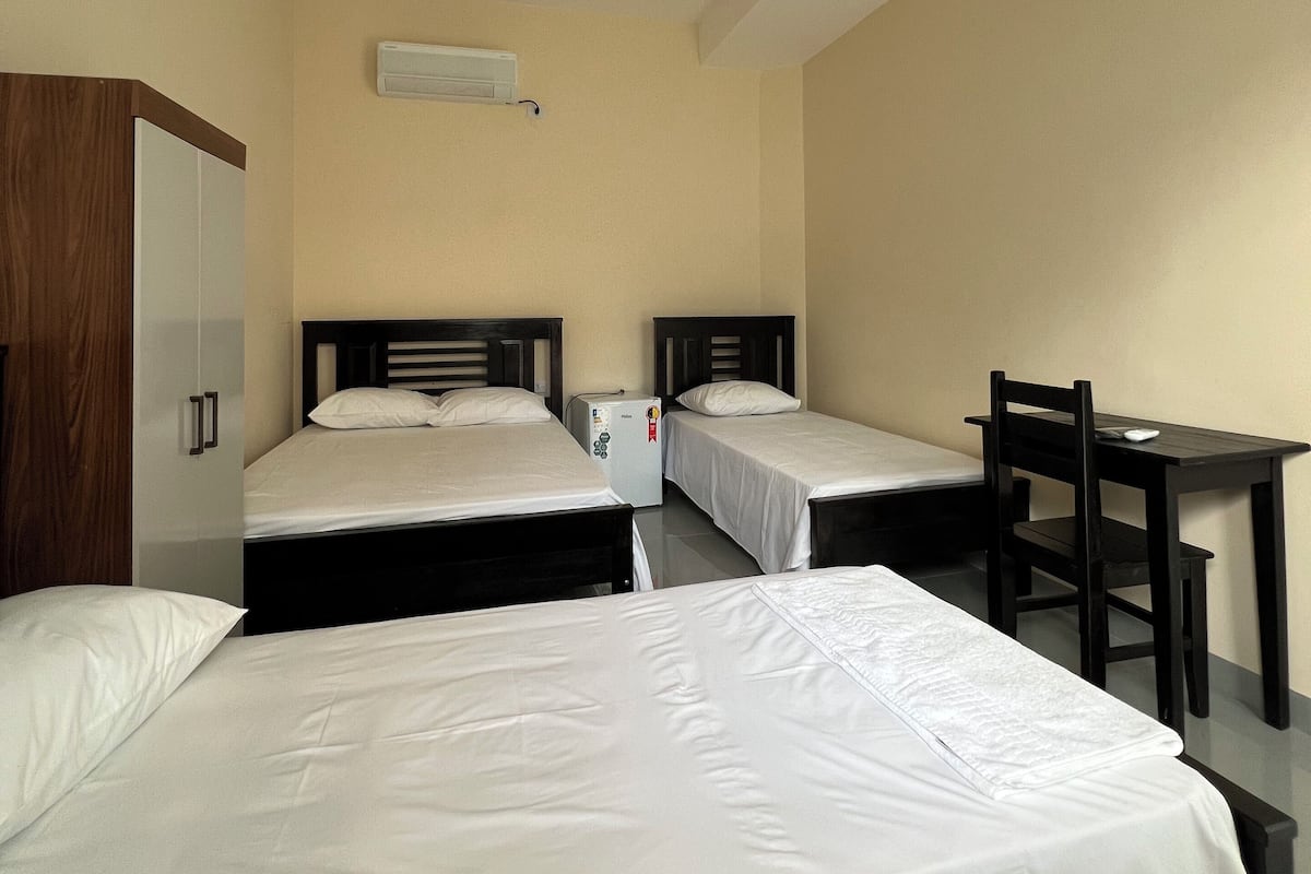 Quarto com três camas de solteiro, uma escrivaninha com cadeira e um pequeno frigorífico.