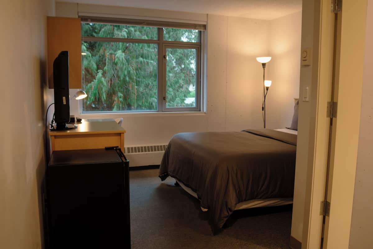 Quarto com cama, escrivaninha com computador, janela e abajur.