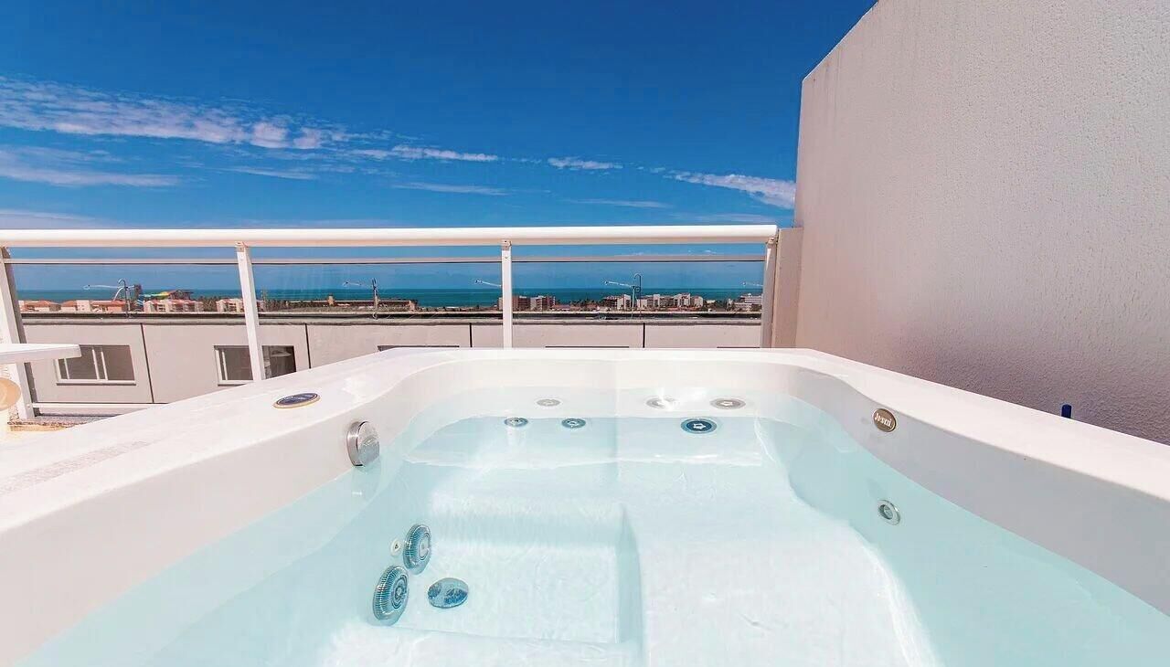 Banheira de hidromassagem em varanda com vista desimpedida para o mar e edifícios ao fundo.