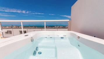 Banheira de hidromassagem em varanda com vista desimpedida para o mar e edifícios ao fundo.