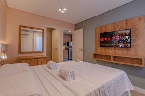 Quarto de hotel com uma cama grande, cabeceira de madeira, TV fixada na parede exibindo Netflix e um espelho sobre a cama.