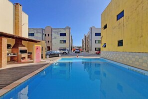 Piscina com deck de madeira, cercada por edifícios com varandas e janelas.