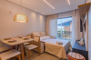 Quarto de hotel moderno com área de refeições, cama com vista e varanda com televisão.