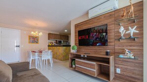 Uma sala de estar moderna com televisão de tela plana, móvel para entretenimento de madeira e um espaço de refeições com cadeiras brancas e uma mesa.