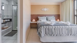 Quarto de hotel com cama, mesa de cabeceira, objeto decorativo na parede e banheiro com chuveiro e vaso sanitário.