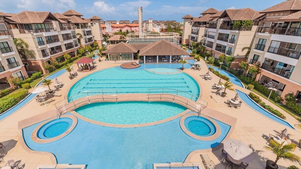 Um resort com uma ampla piscina central, várias varandas e áreas de estar ao ar livre.