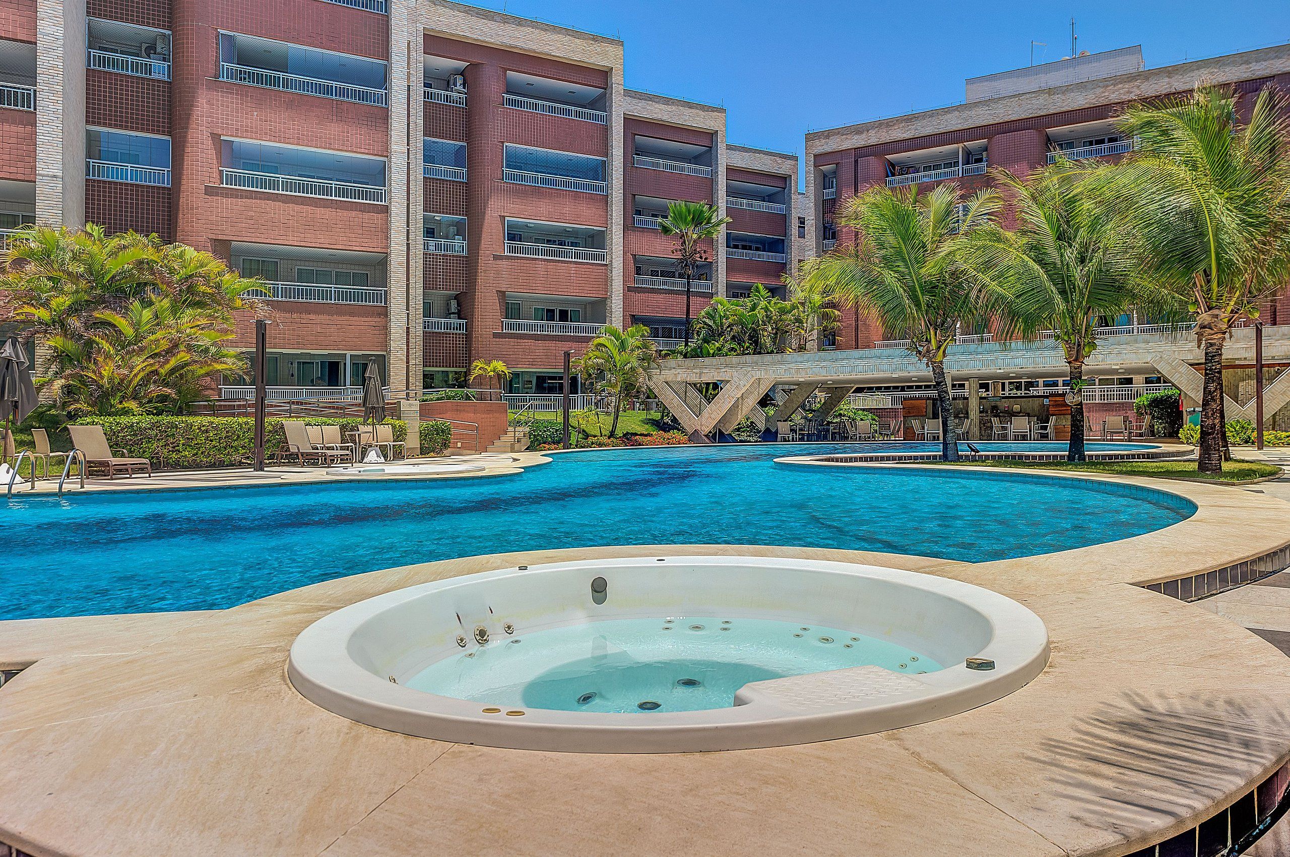 Um hotel com piscina, banheira de hidromassagem e um deck com palmeiras.