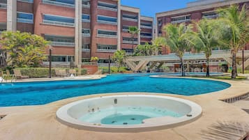 Um hotel com piscina, banheira de hidromassagem e um deck com palmeiras.