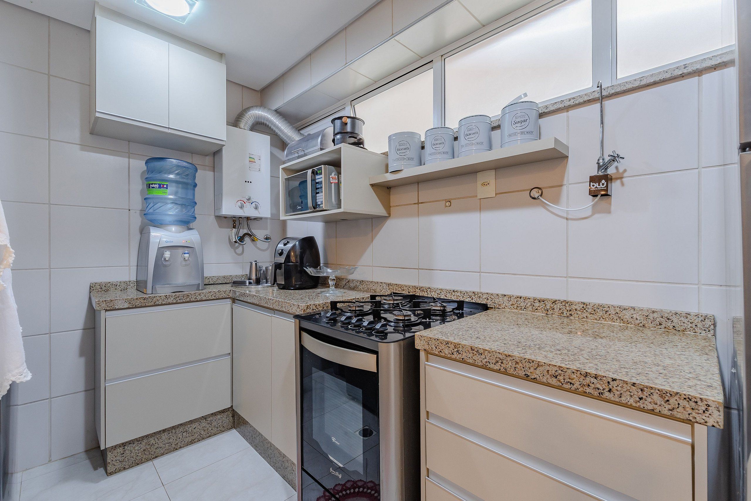 Cozinha compacta com fogão a gás, bebedouro e micro-ondas.