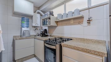 Cozinha compacta com fogão a gás, bebedouro e micro-ondas.