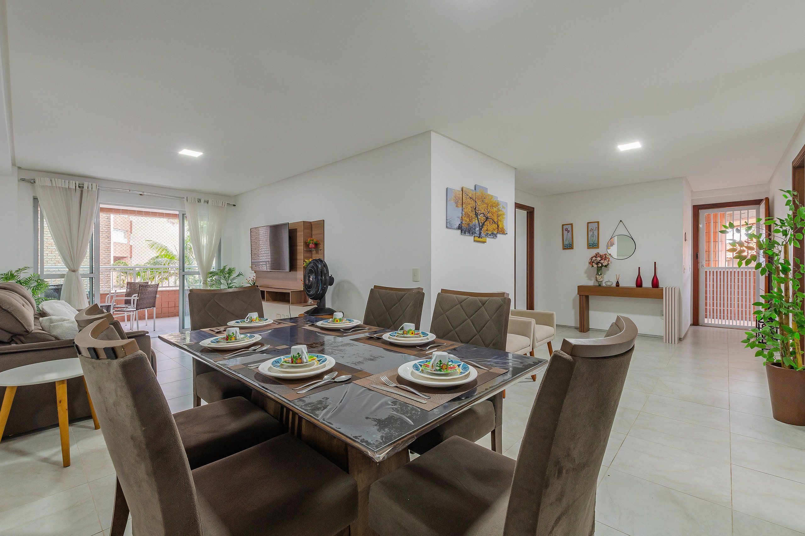 Uma área de refeições com uma mesa retangular posta para quatro pessoas, rodeada por cadeiras estofadas.
