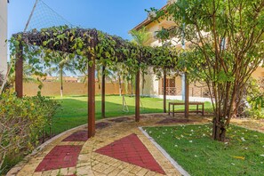 Um pátio com caminho de tijolos, uma pérgola coberta por trepadeiras e uma pequena árvore.
