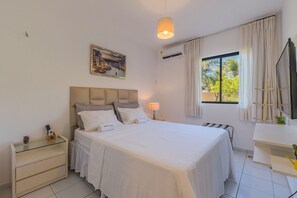 Quarto de hotel com cama, mesa de cabeceira, luminária e um quadro na parede.