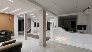 Uma área de recepção moderna de hotel, com um balcão curvo, um sofá e uma escadaria ao fundo.