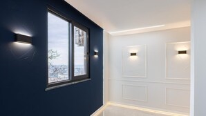Um corredor com uma janela grande, iluminação embutida na parede e piso revestido com azulejos.