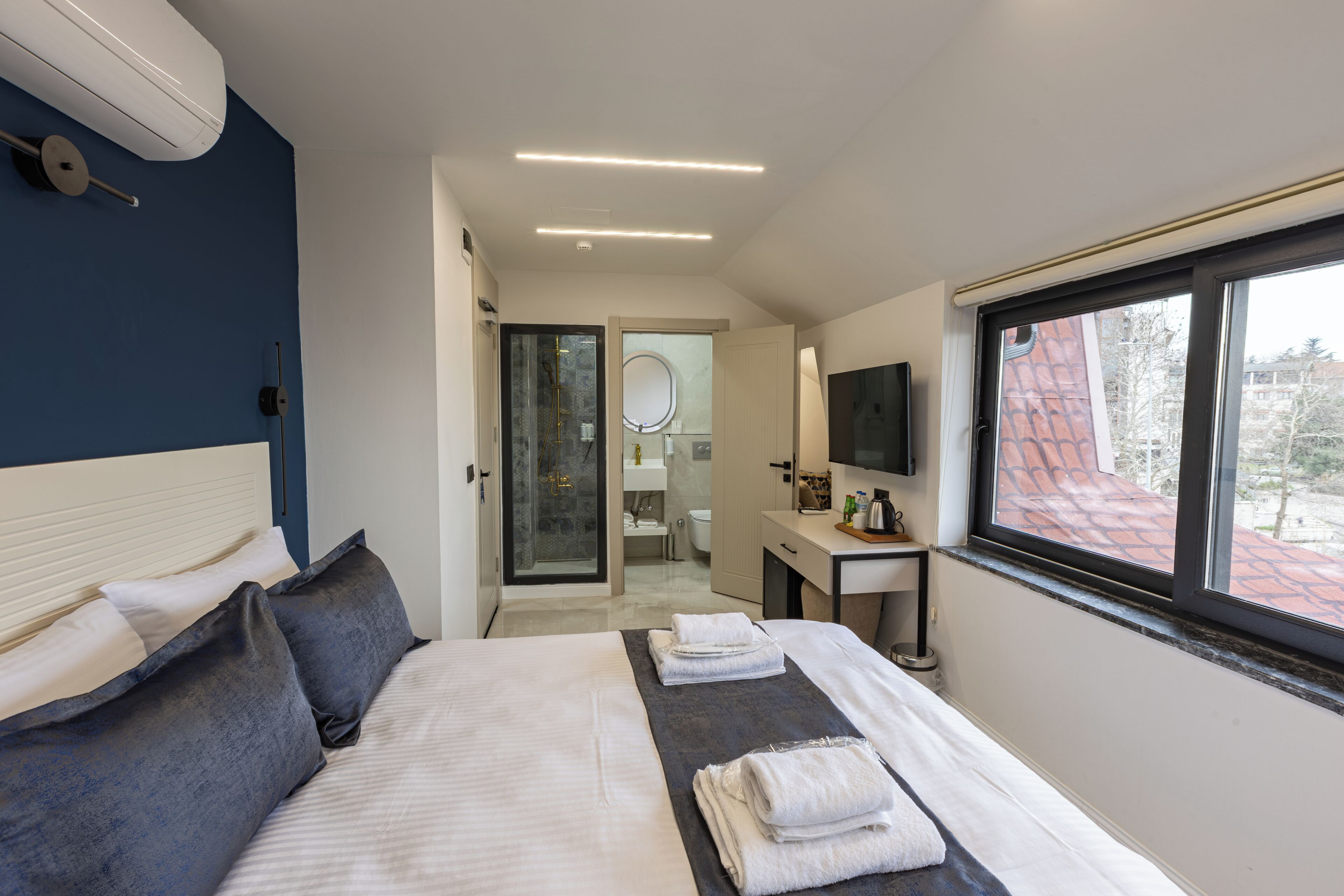 Quarto de hotel com cama, escrivaninha, televisão e janela.
