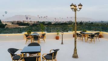 Terraço no telhado com área de estar externa, um poste de luz e balões de ar quente ao longe.