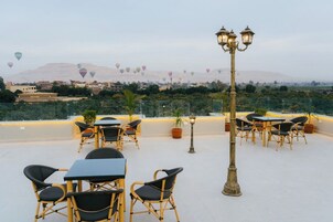 Terraço no telhado com área de estar externa, um poste de luz e balões de ar quente ao longe.